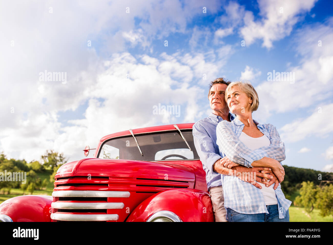 Senior couple hugging, vintage styled red car, sunny nature Stock Photo ...