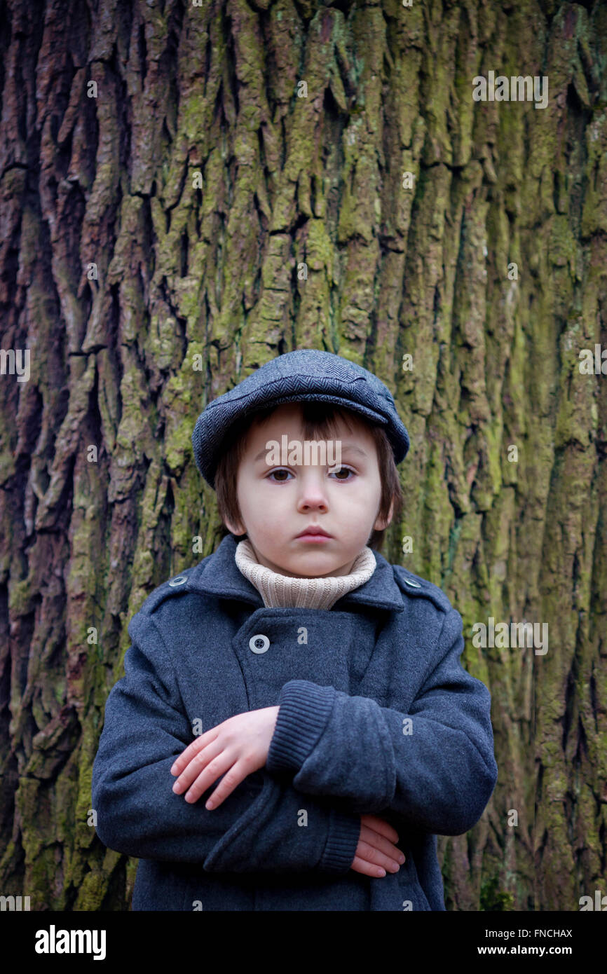 Close portrait of a little boy in the forest, standing next to a tree ...