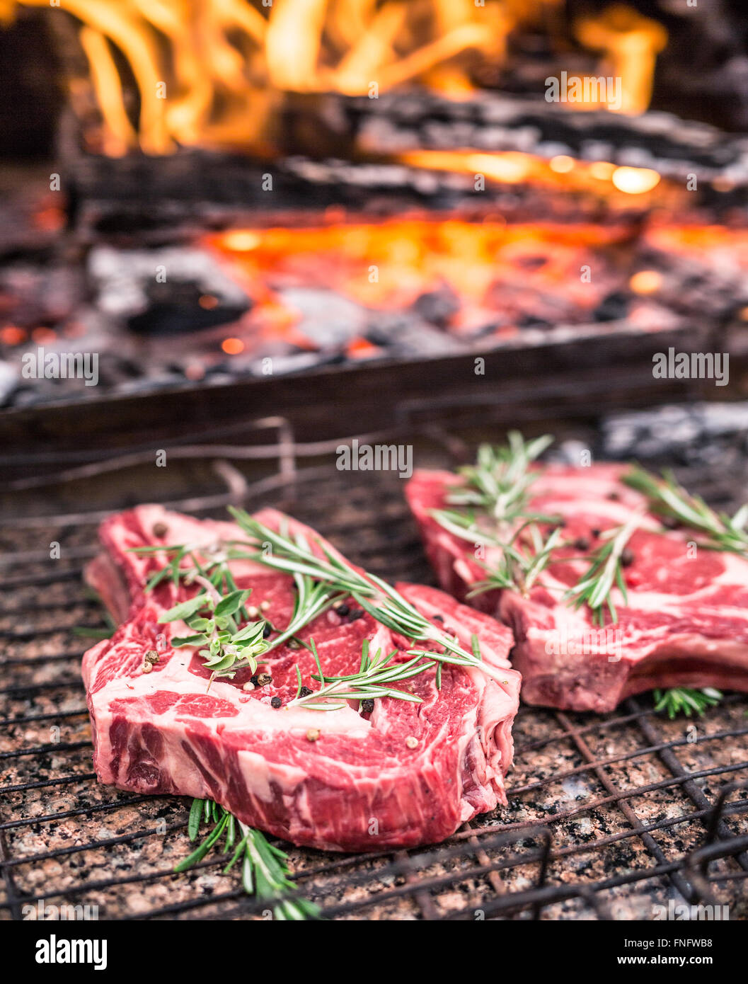 Rib eye steaks and grill with burning fire behind them Stock Photo - Alamy