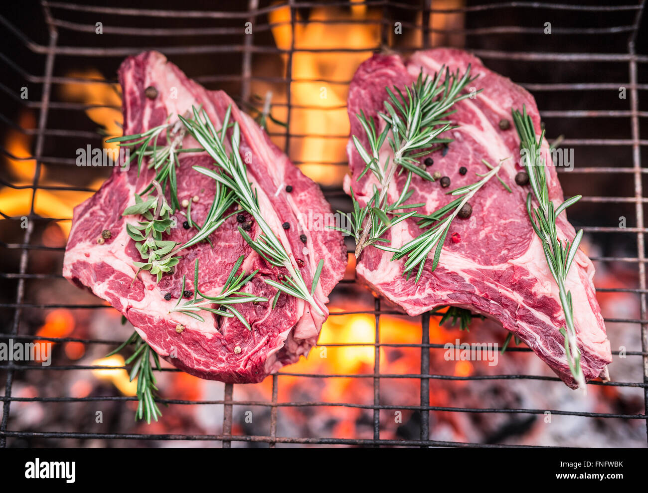 Rib eye steaks and grill with burning fire behind them Stock Photo - Alamy