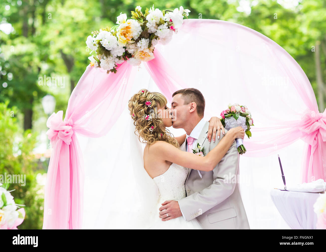 Happy newlywed romantic couple kissing at wedding aisle with pink ...