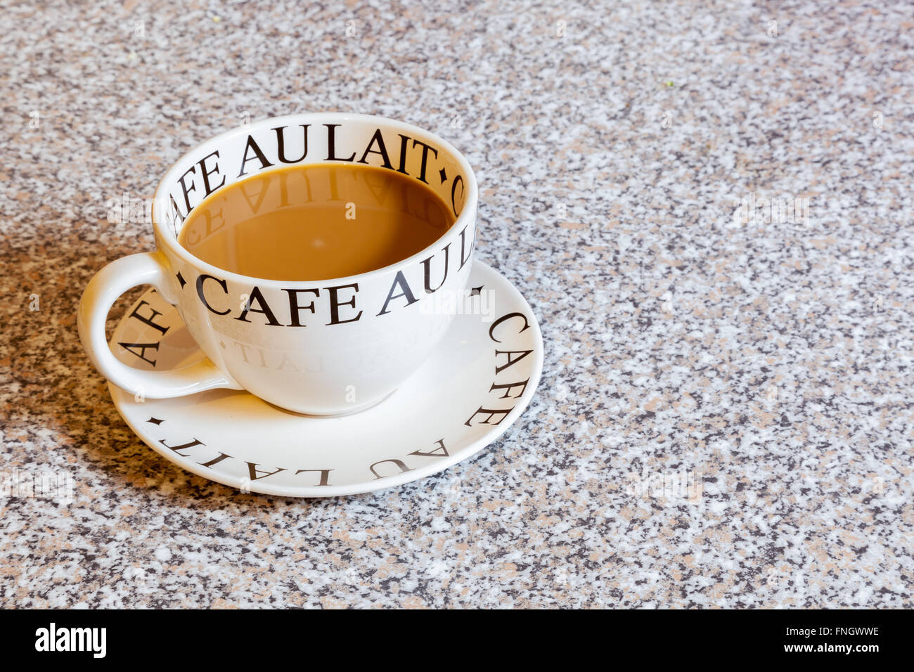 A large round cup of white coffee on a matching saucer on a granite ...