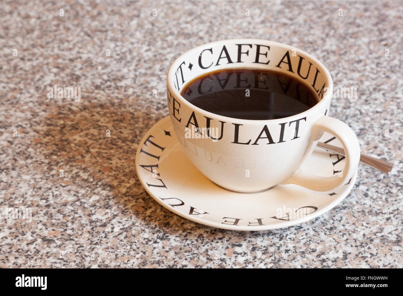 A large round cup of black coffee on a matching saucer with a spoon on ...