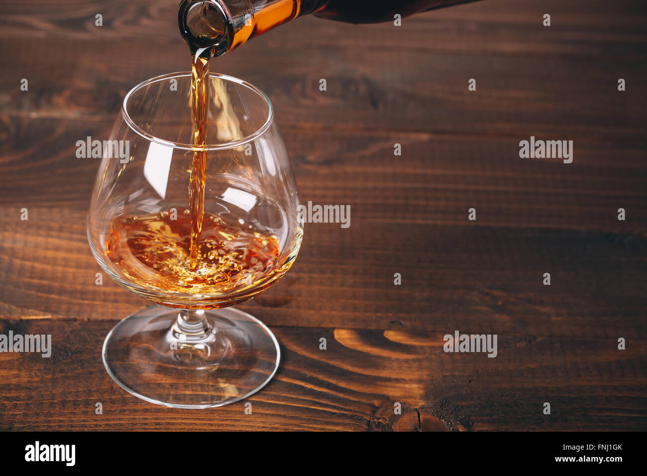 Pouring brandy or cognac from the bottle into the glass against wooden ...