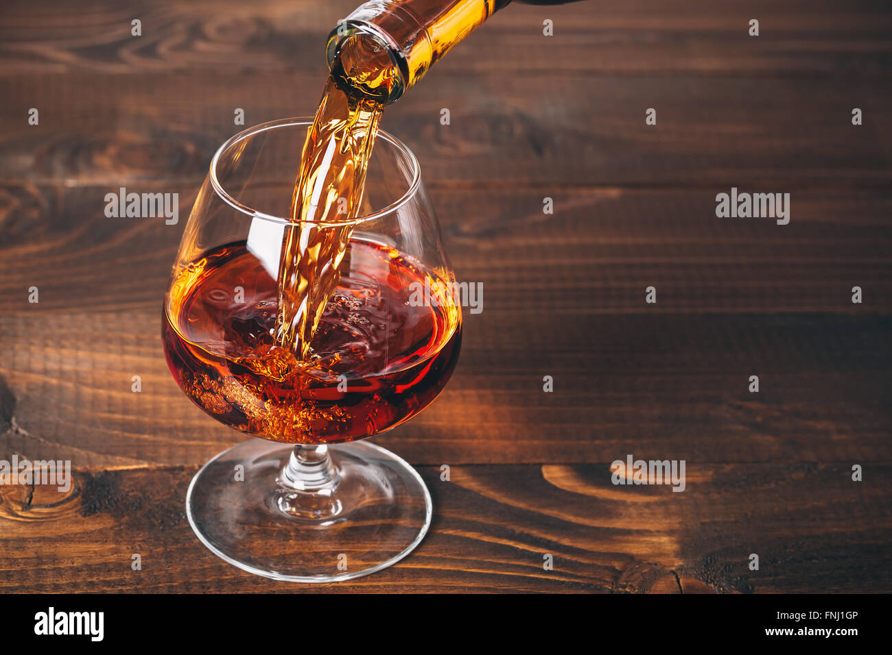 Pouring brandy or cognac from the bottle into the glass against wooden ...