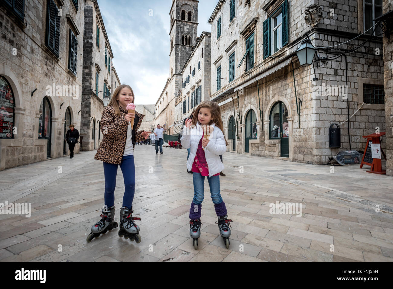 Two girls skating and eating ice-cream in the old city of Dubrovnik ...