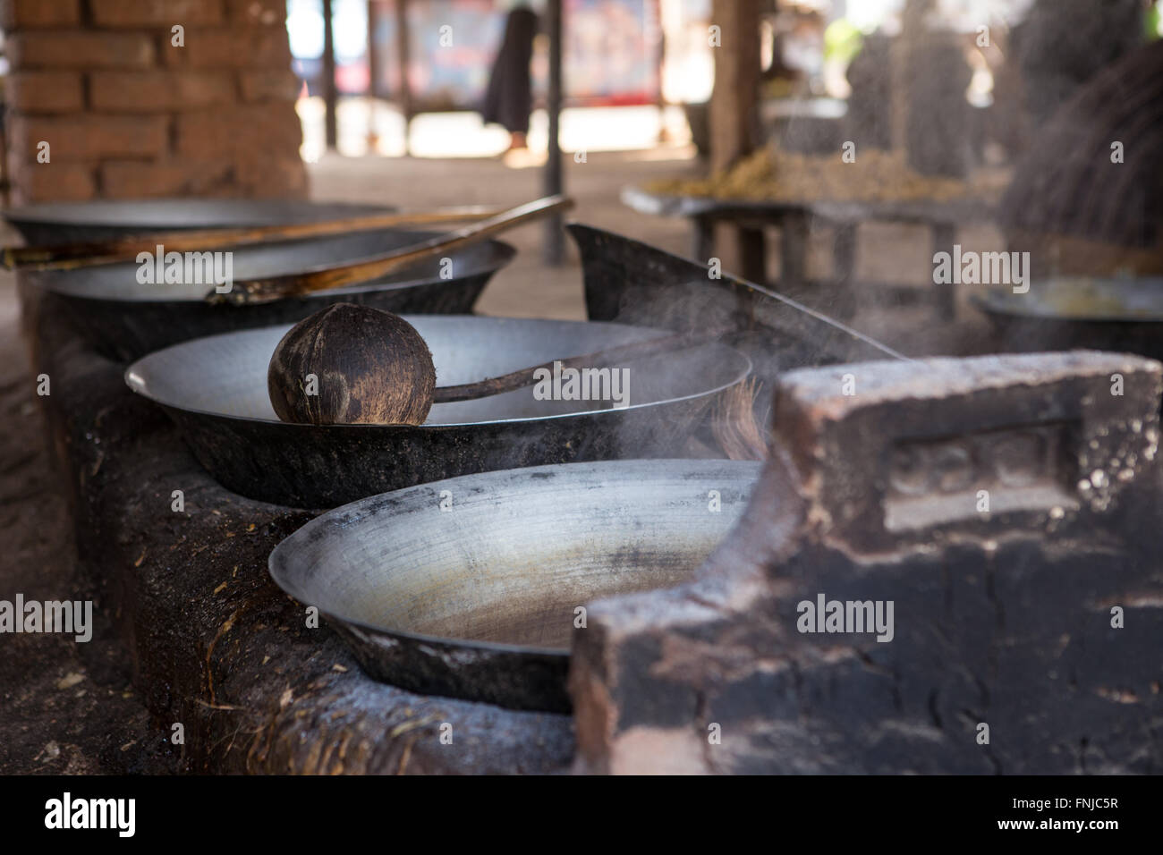 Four metal woks with ladles over fire cooking and converting palm oil ...