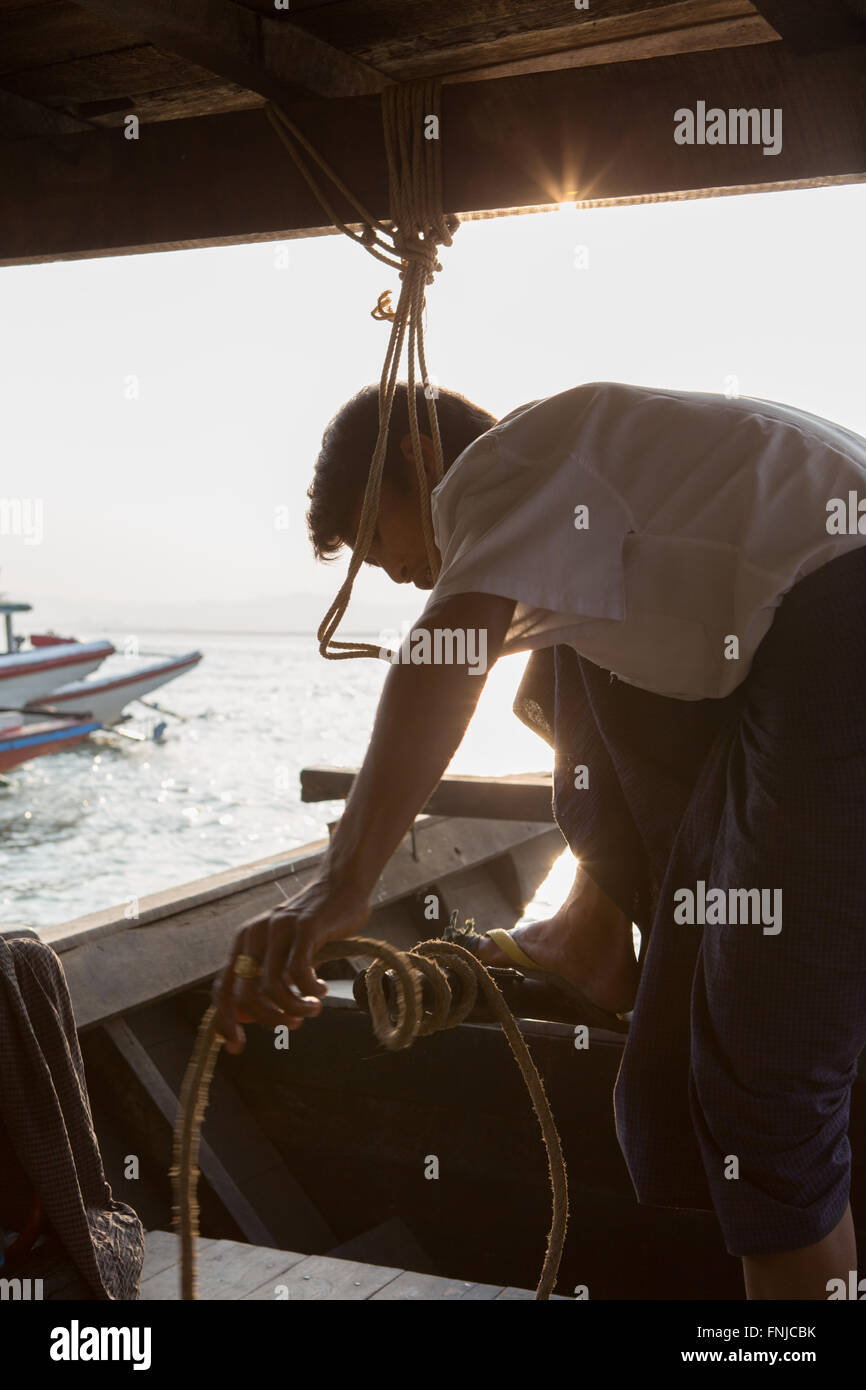 Young Burmese local operating a boat during sunset cruise on Irrawaddy ...
