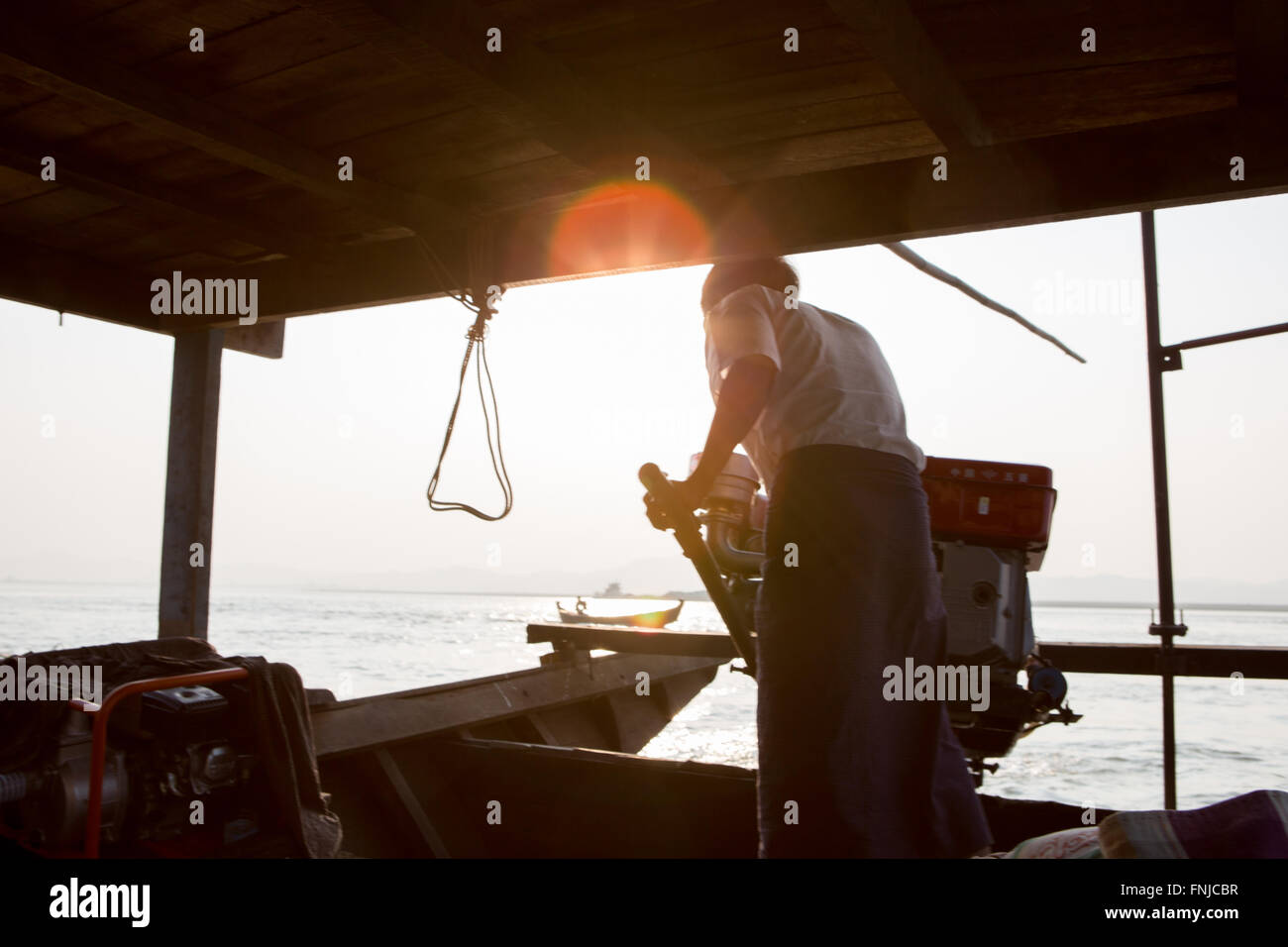 Young Burmese local operating a boat during sunset cruise on Irrawaddy ...