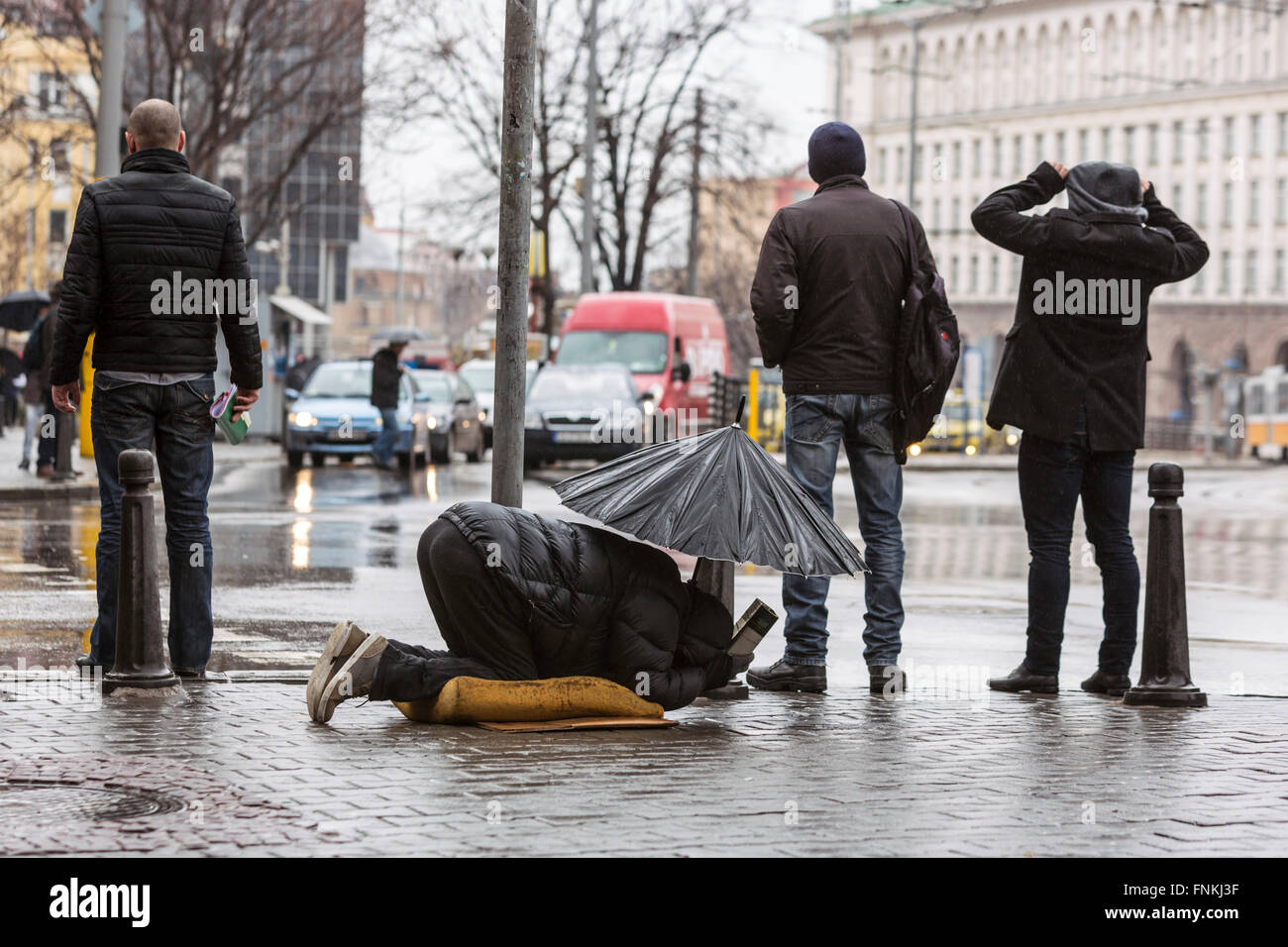 Homeless beggar is begging with umbrella in the rain near a walkway at ...
