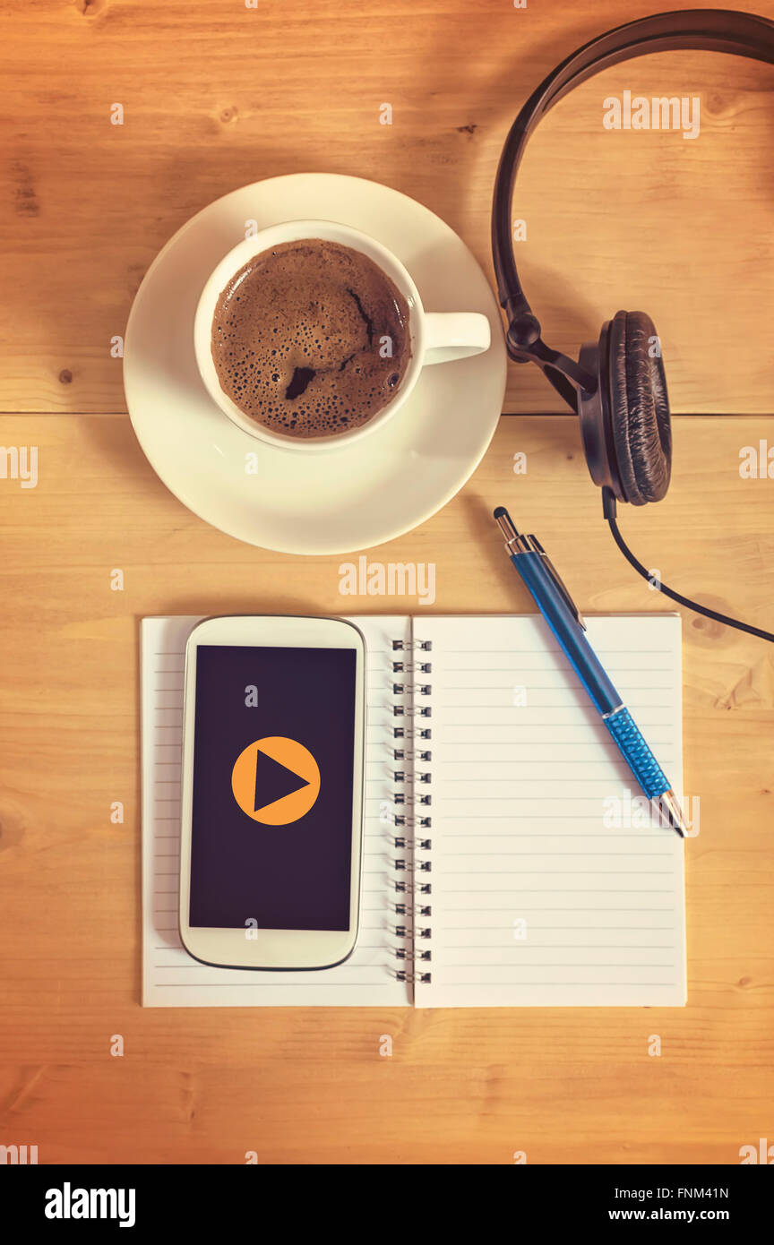 Play button on smart phone with headset, notebook, pencil, coffee cup ...