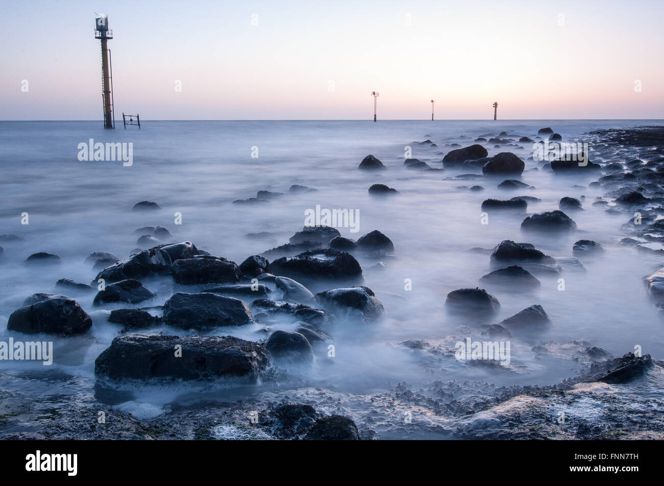Sunset at beach with boulders and masts in the water Stock Photo - Alamy