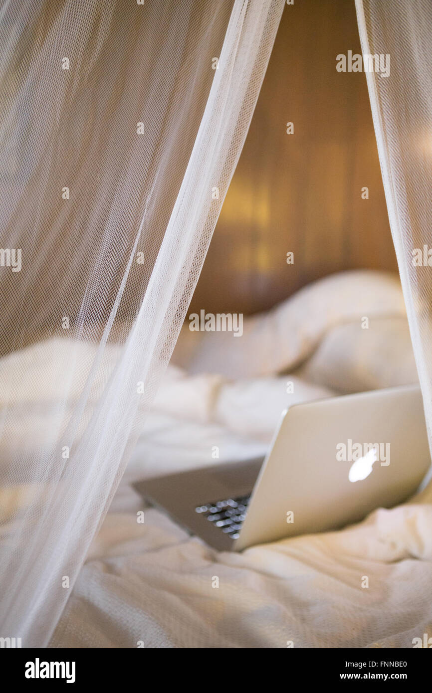 Laptop computer on messy bed with mosquito net canopy in eco-resort in ...