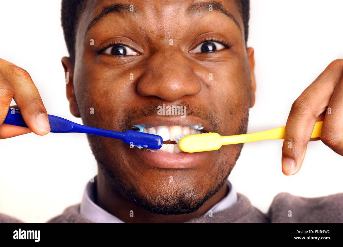 Young man brushing teeth with two toothbrushes Stock Photo - Alamy