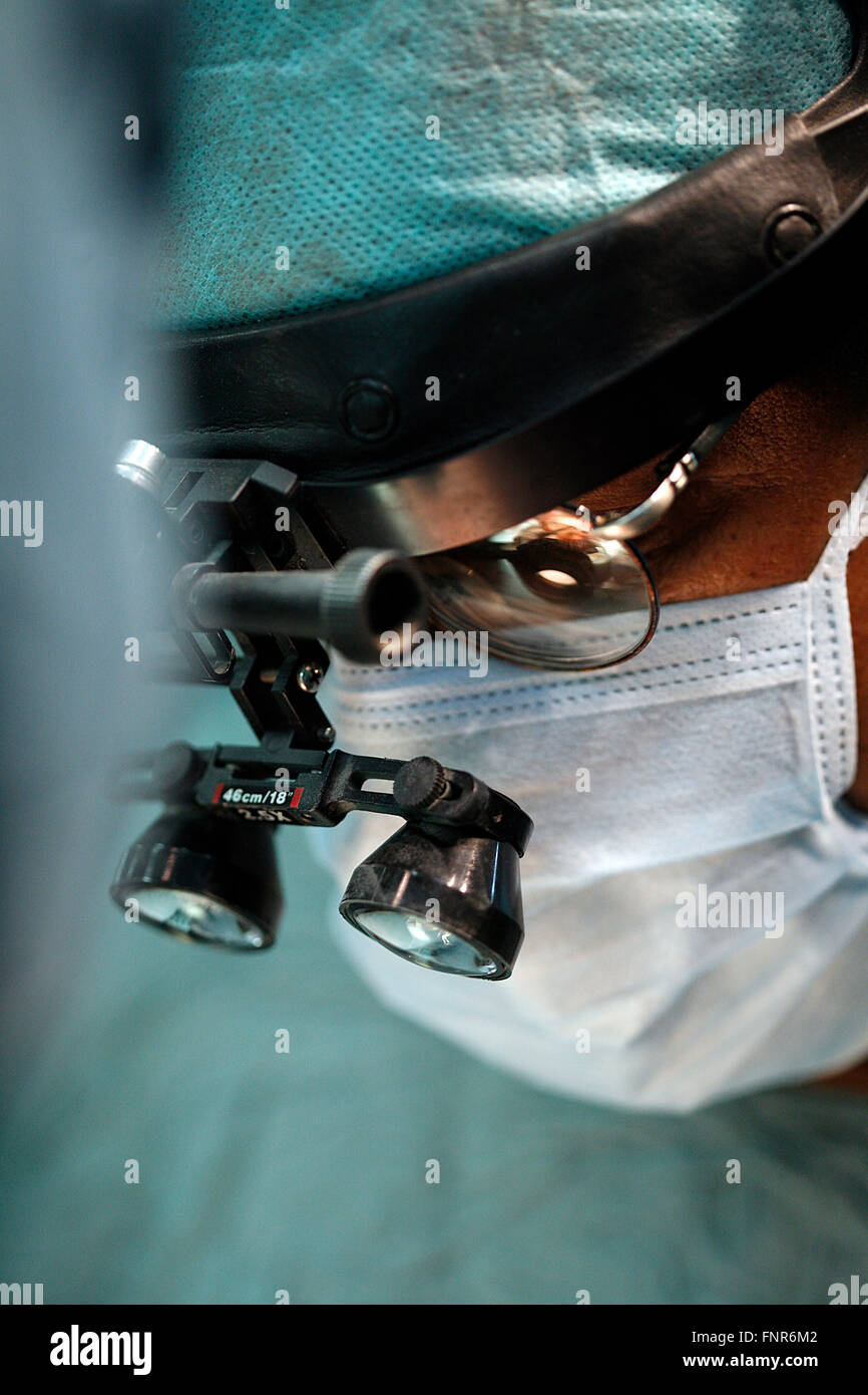 A heart surgeon wears magnifying lenses over his glasses. The ...