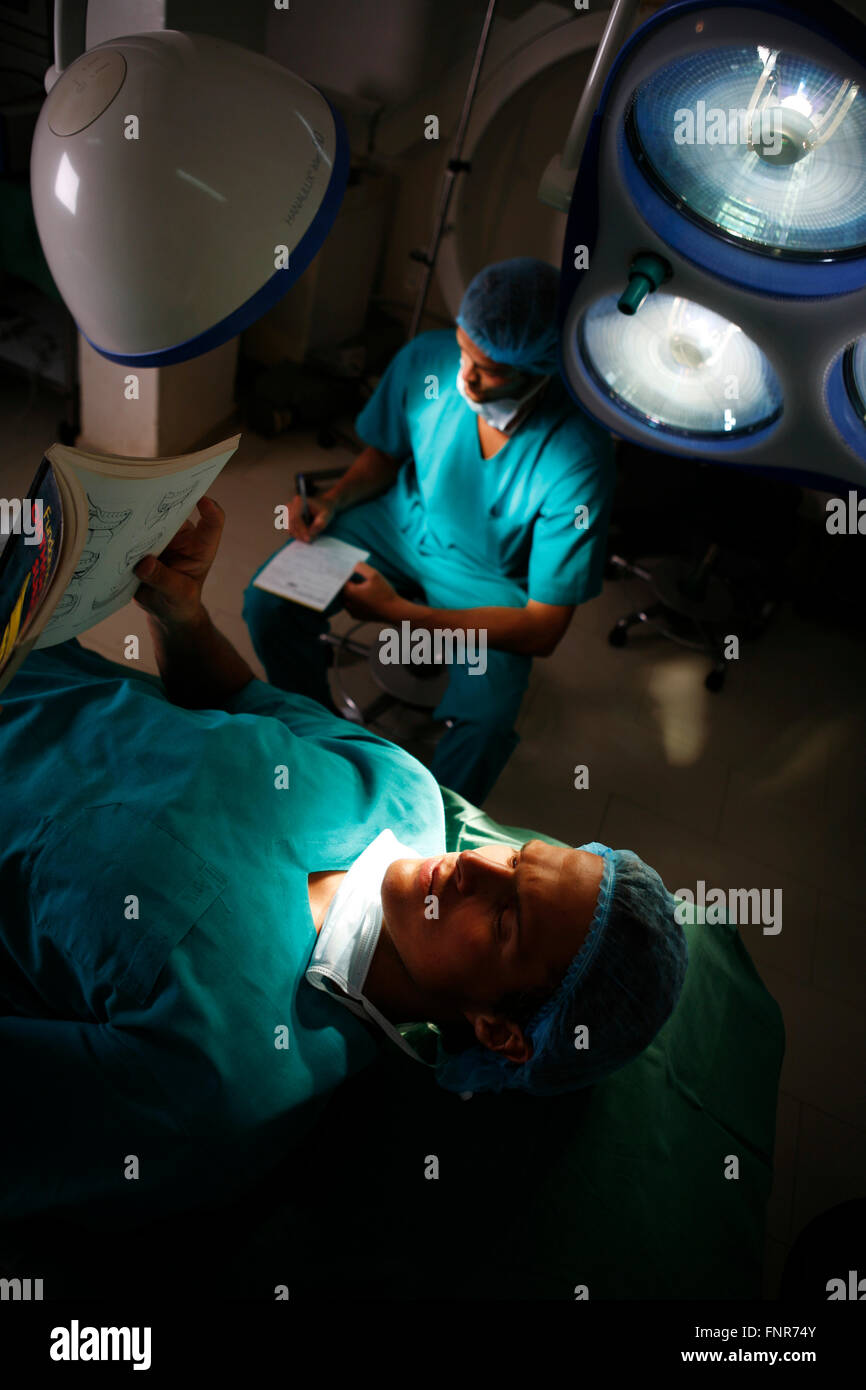 A surgeon reading a book whilst laying on an operating table. A second ...