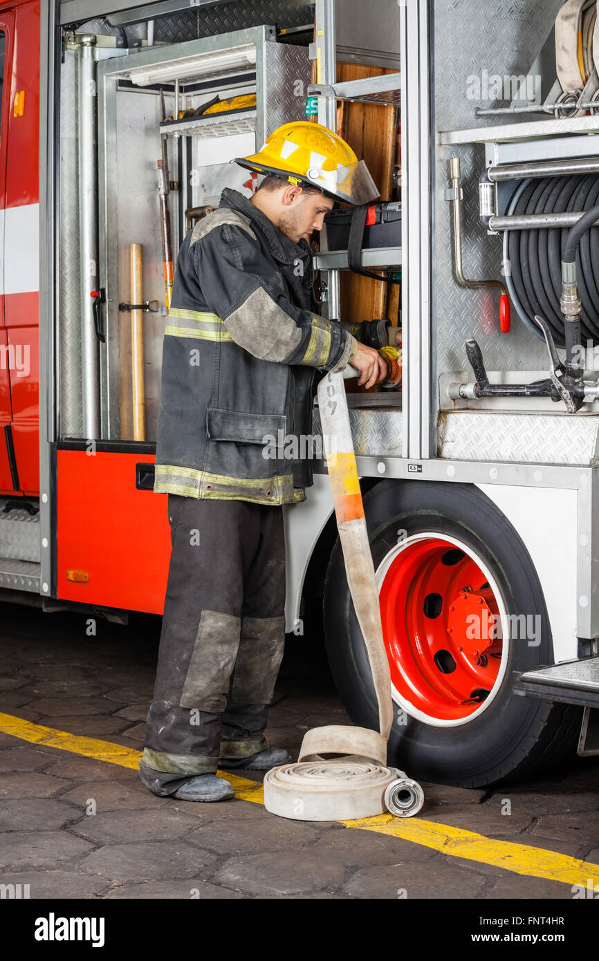 Full length of male firefighter fixing water hose in truck at fire ...
