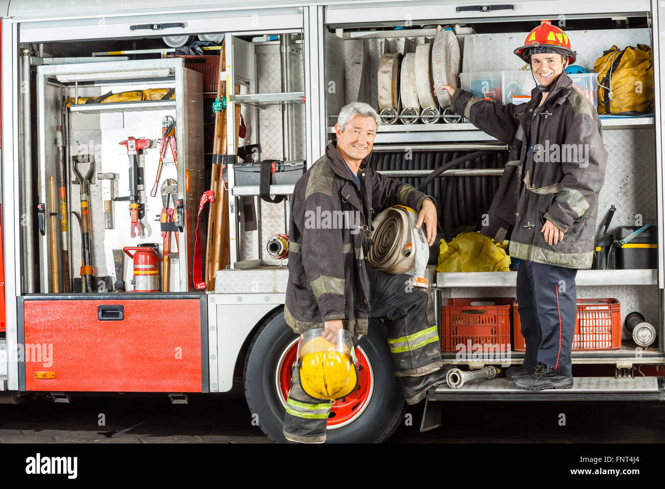 Portrait of confident male firefighters standing on truck at fire ...