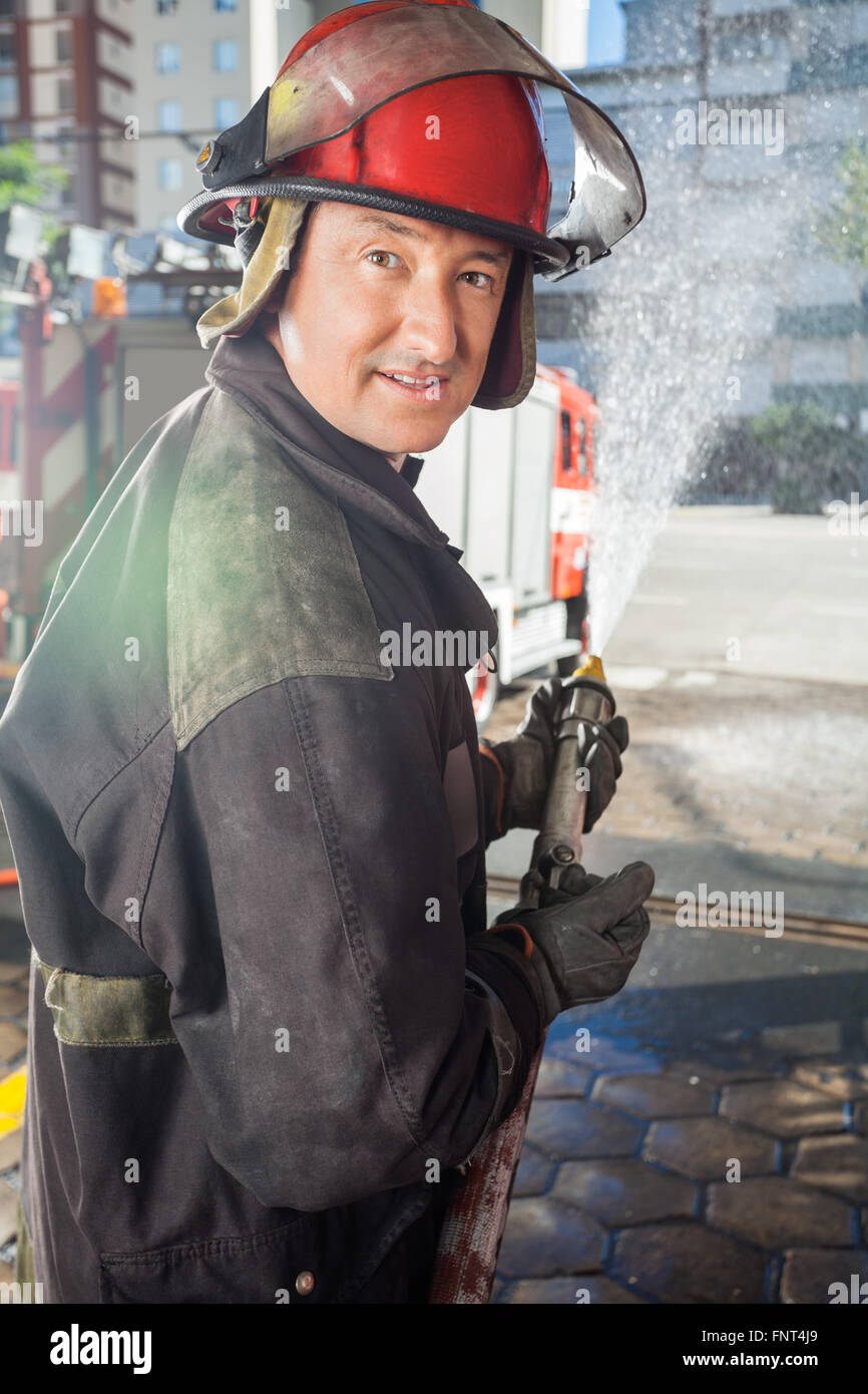Side view portrait of smiling mature fireman spraying water during ...