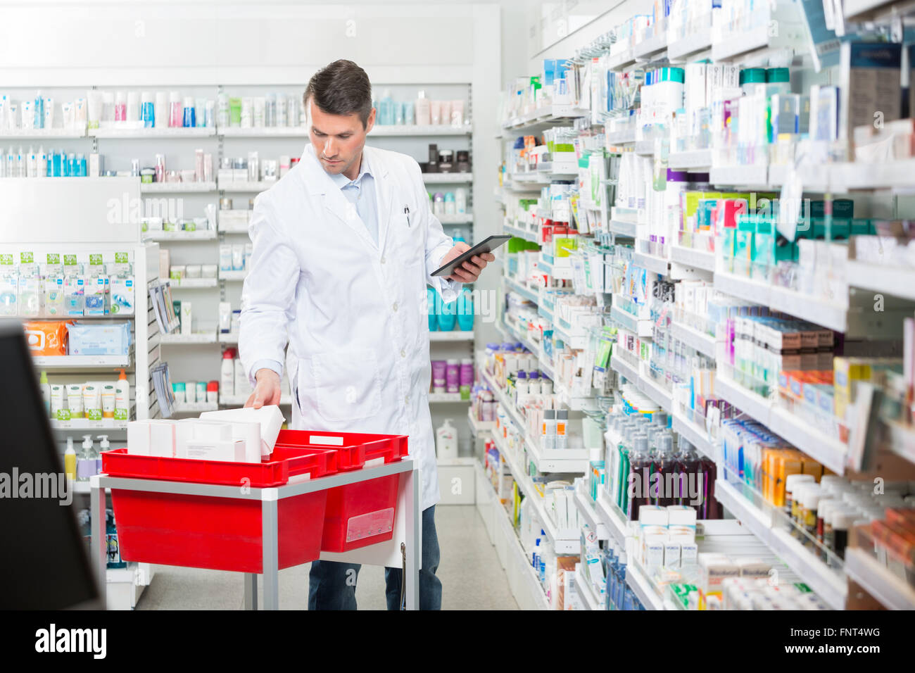 Mid adult male pharmacist counting stock while holding digital tablet ...