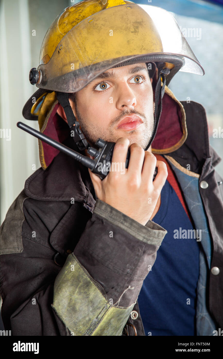 Confident male fireman looking away while using walkie talkie at fire ...