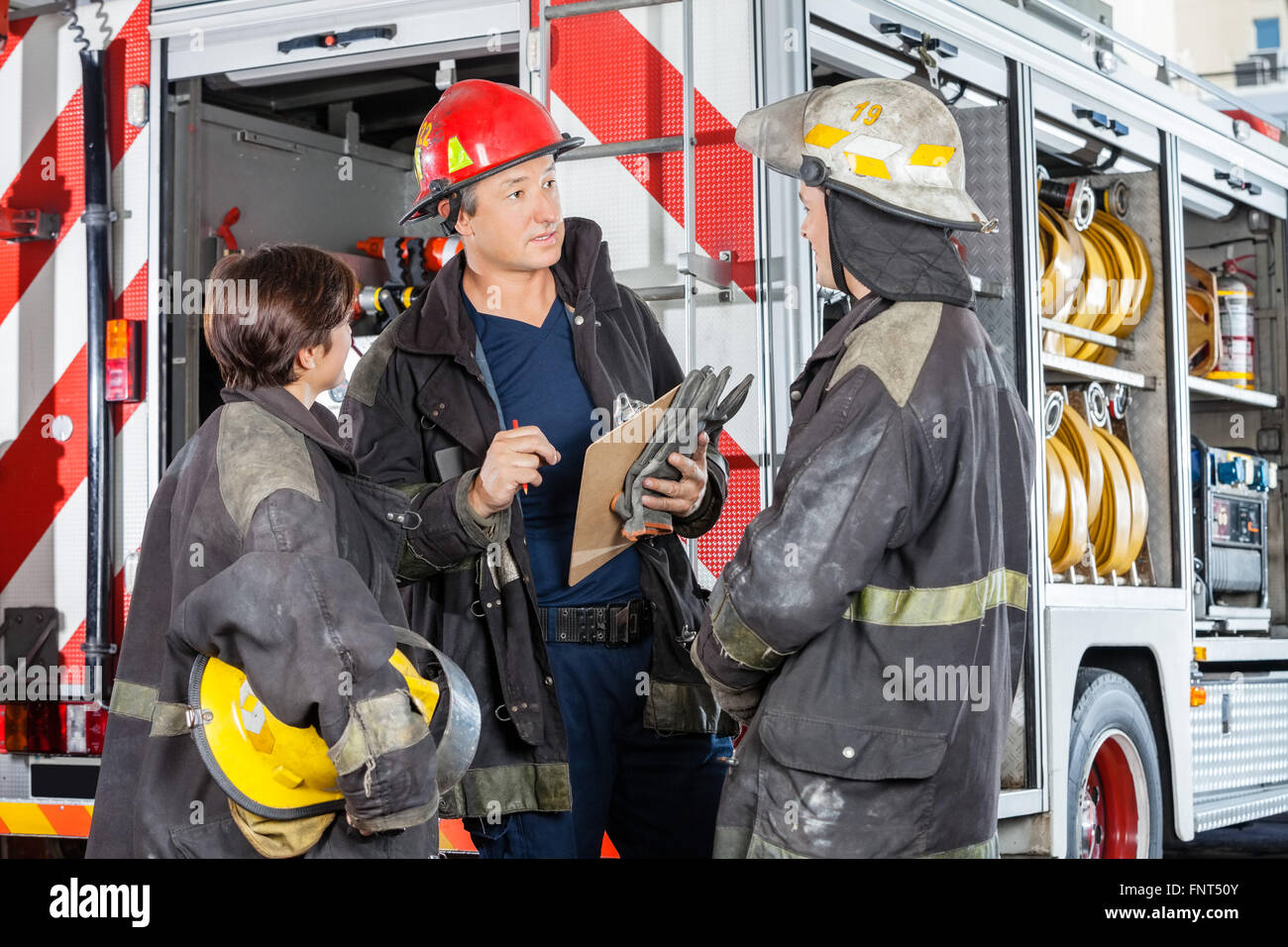 Male and female firefighters discussing while standing against truck at ...
