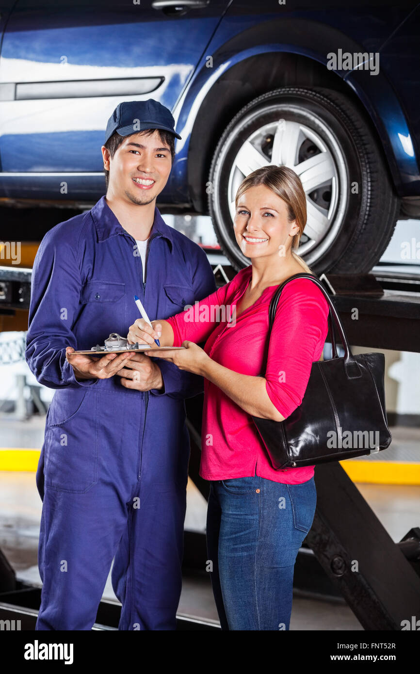 Portrait of happy mechanic with female customer while signing invoice ...