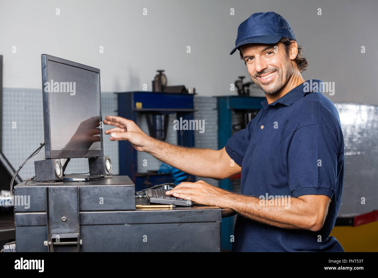 Portrait of happy male mechanic using computer in auto repair shop ...