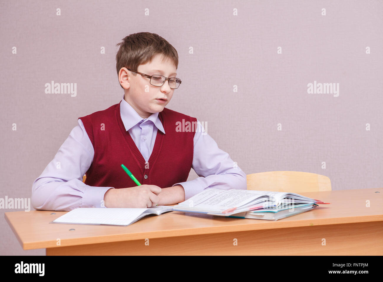 boy with glasses sitting at a desk writing Stock Photo - Alamy
