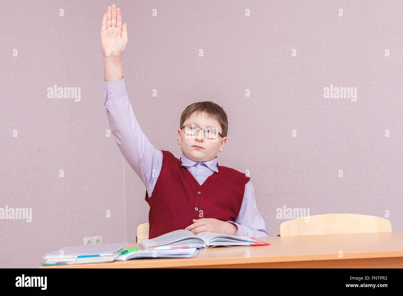 boy pulls a hand up sitting at his desk Stock Photo - Alamy