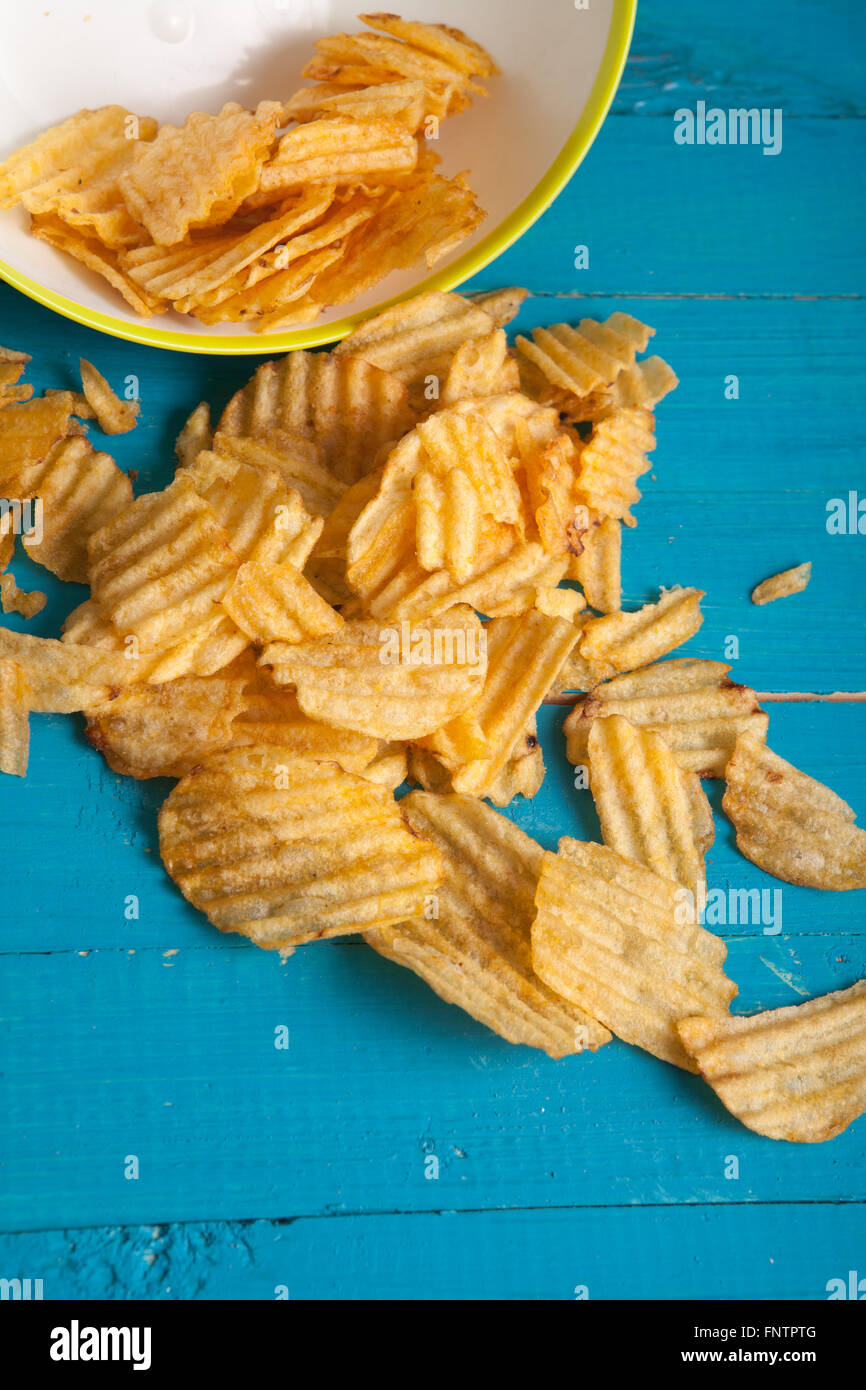 Potato chips poured out of the plate on a blue wooden table Stock Photo ...