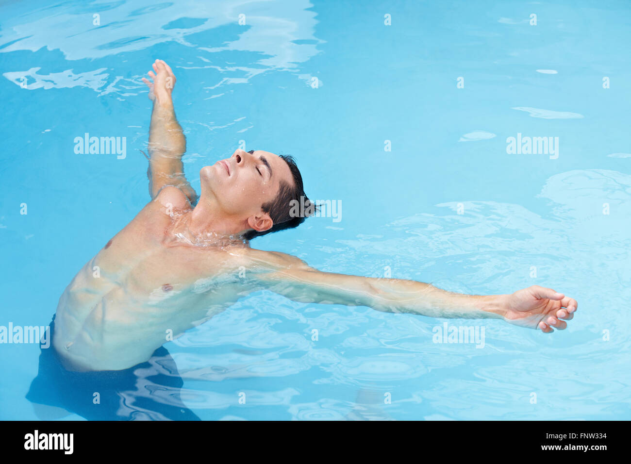 Young attractive man relaxing leaned back in ocean with blue water ...