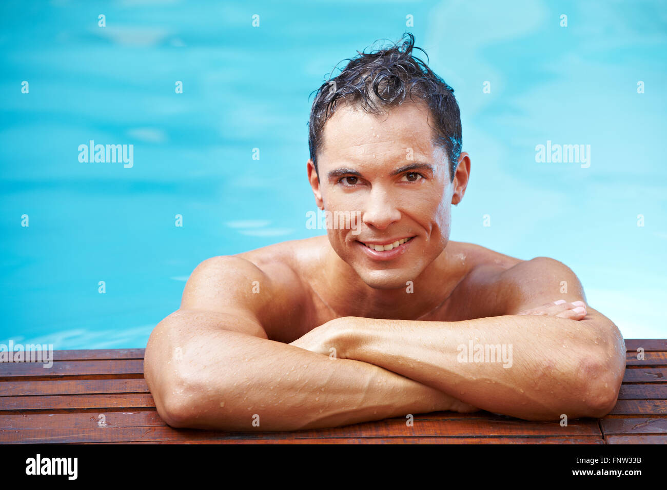 Young smiling man leaning at edge of swimming pool Stock Photo - Alamy