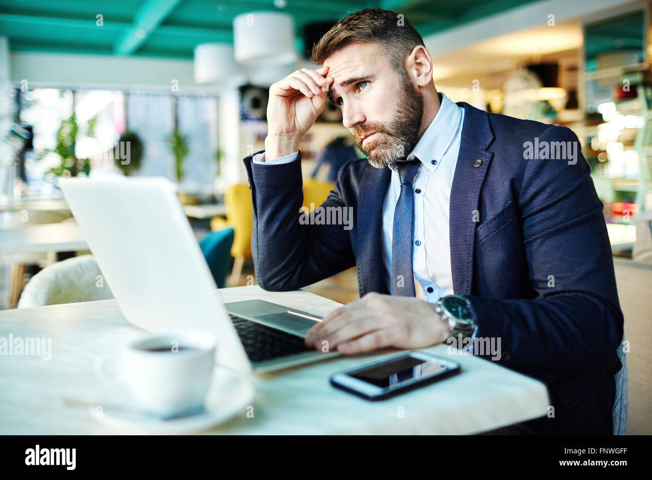Pensive employee sitting in front of laptop by table Stock Photo - Alamy
