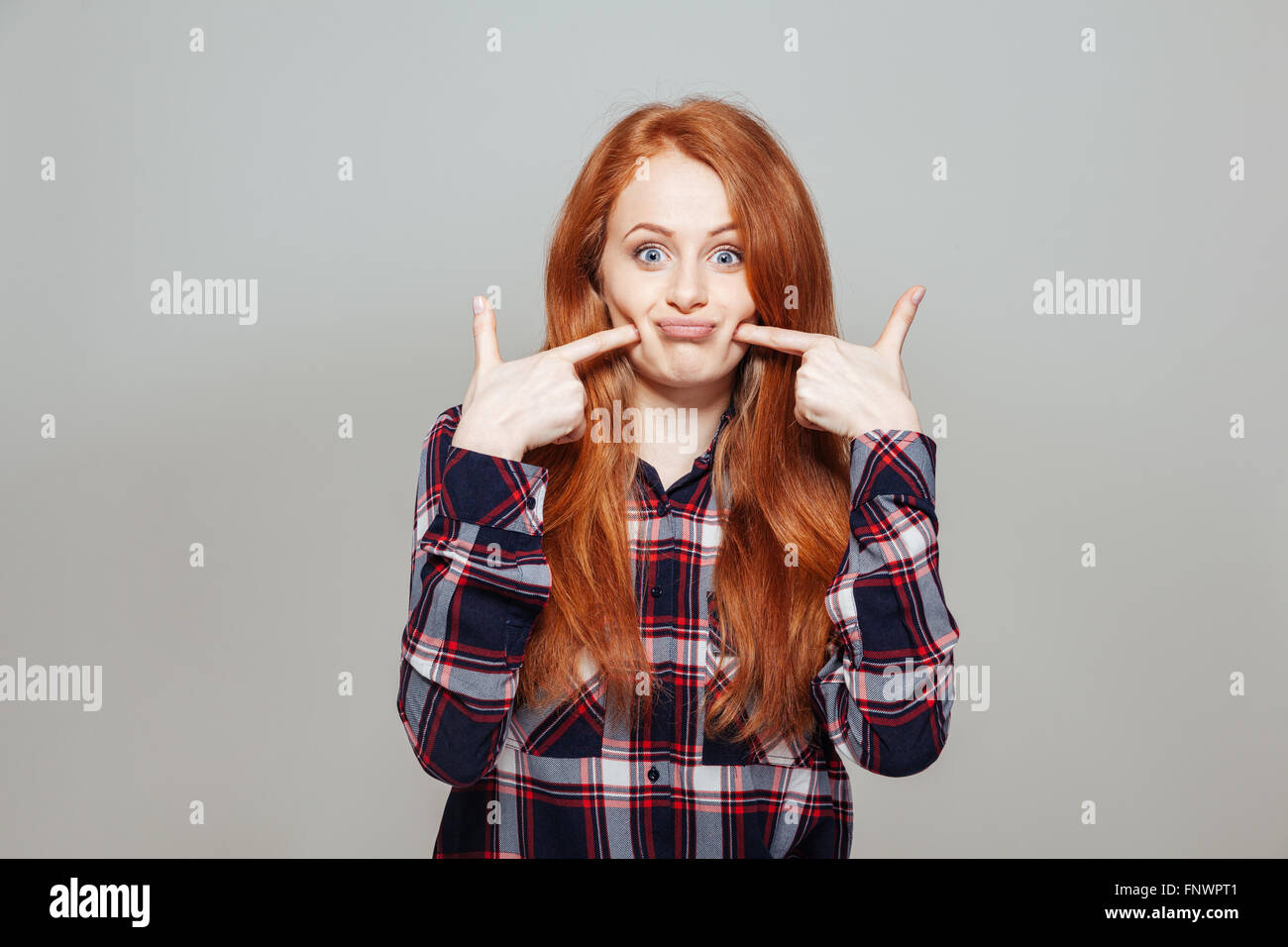 Funny redhead woman pointing finger at her cheek isolated on a white ...