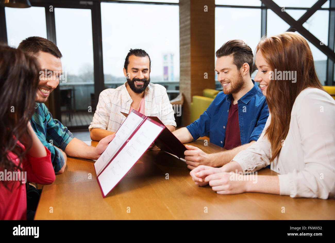 smiling friends discussing menu at restaurant Stock Photo - Alamy