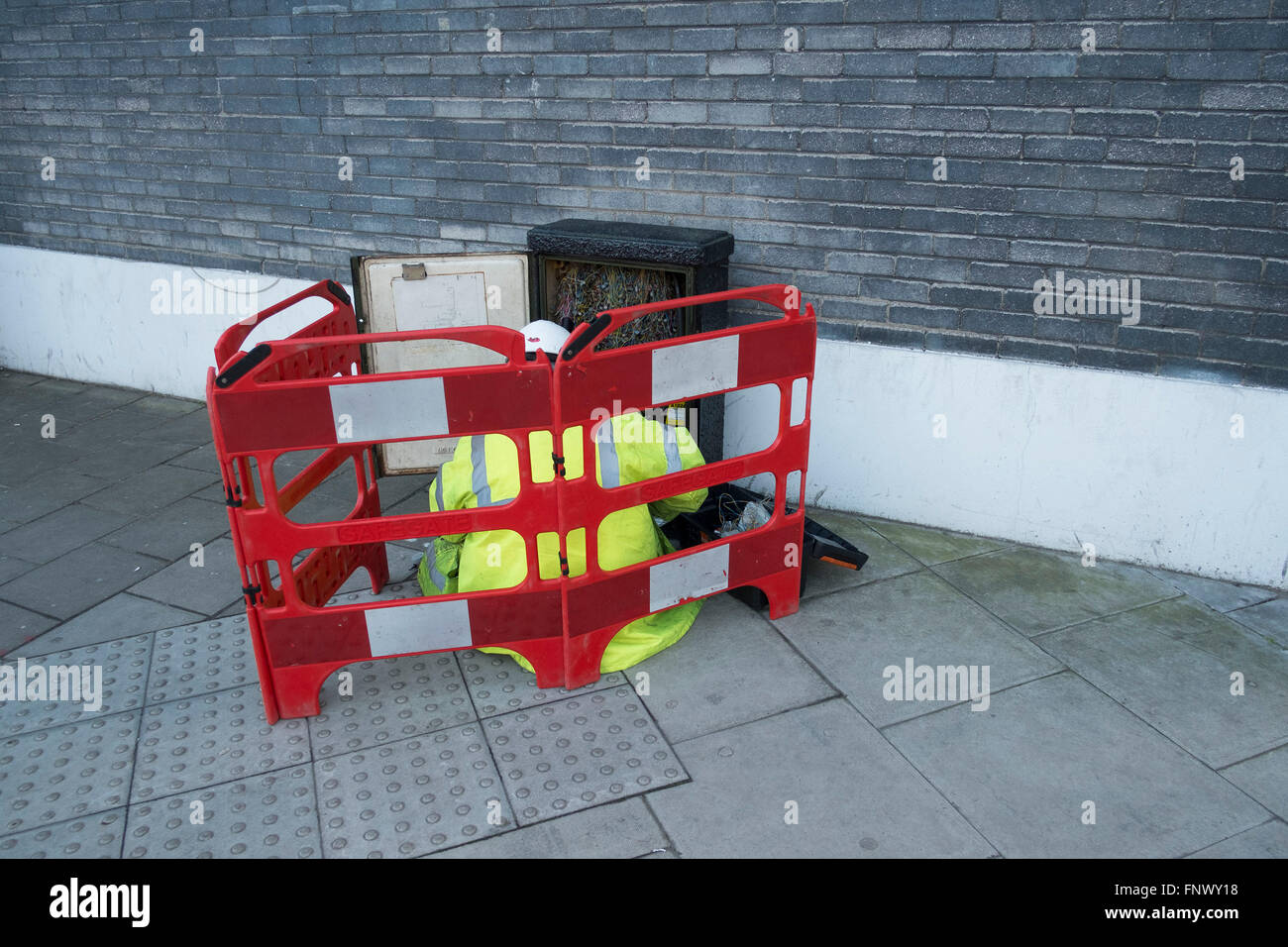 Telecoms workman cordoned off as he works on a telephone exchange box ...