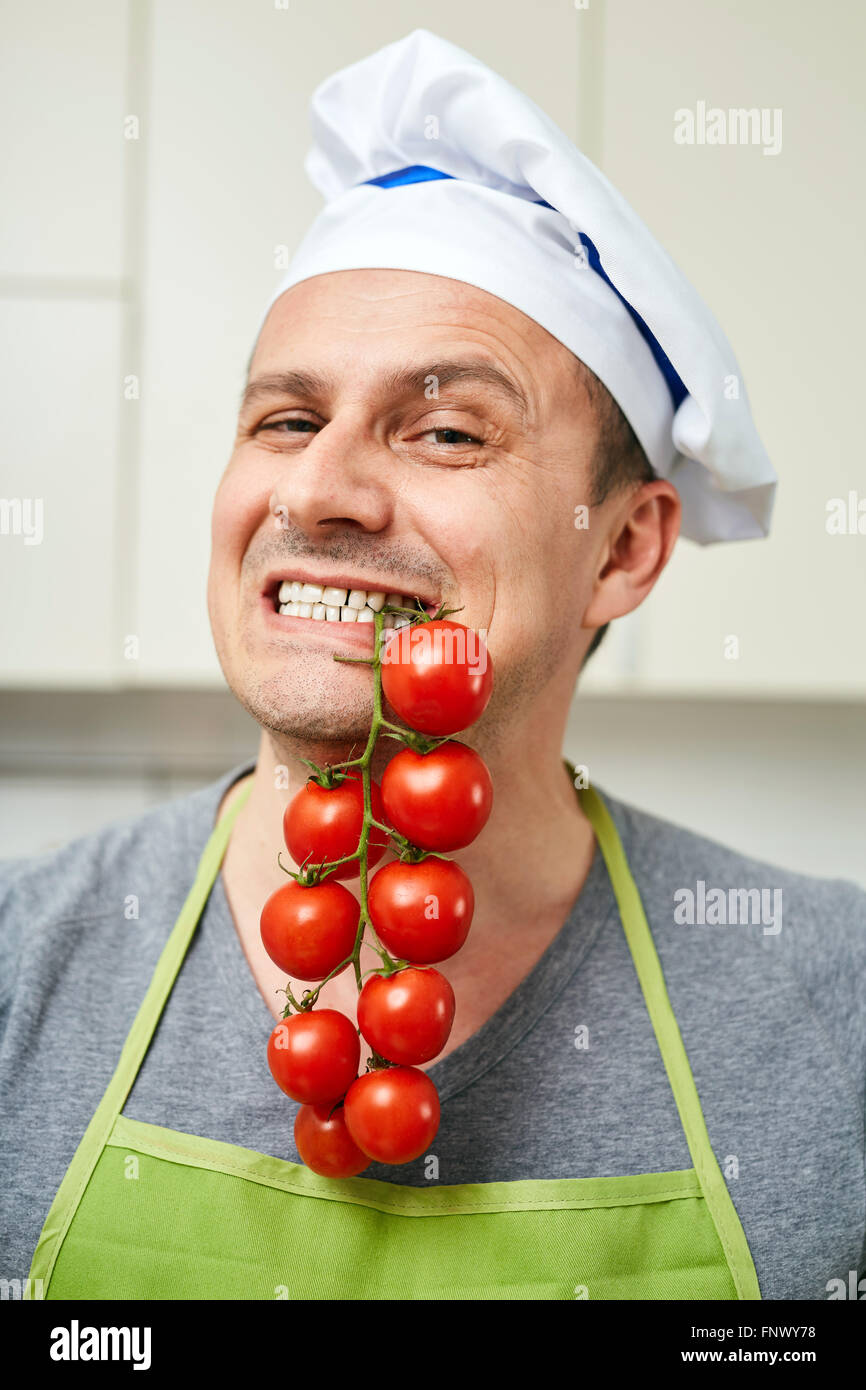 Portrait of a cook holding a bunch of cherry tomatoes in his teeth ...