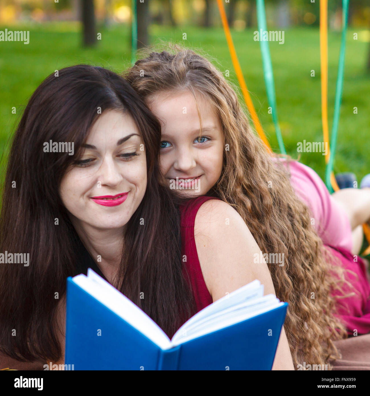 Mom And Daughter Reading A Book Lying On The Plaid In The Park Stock