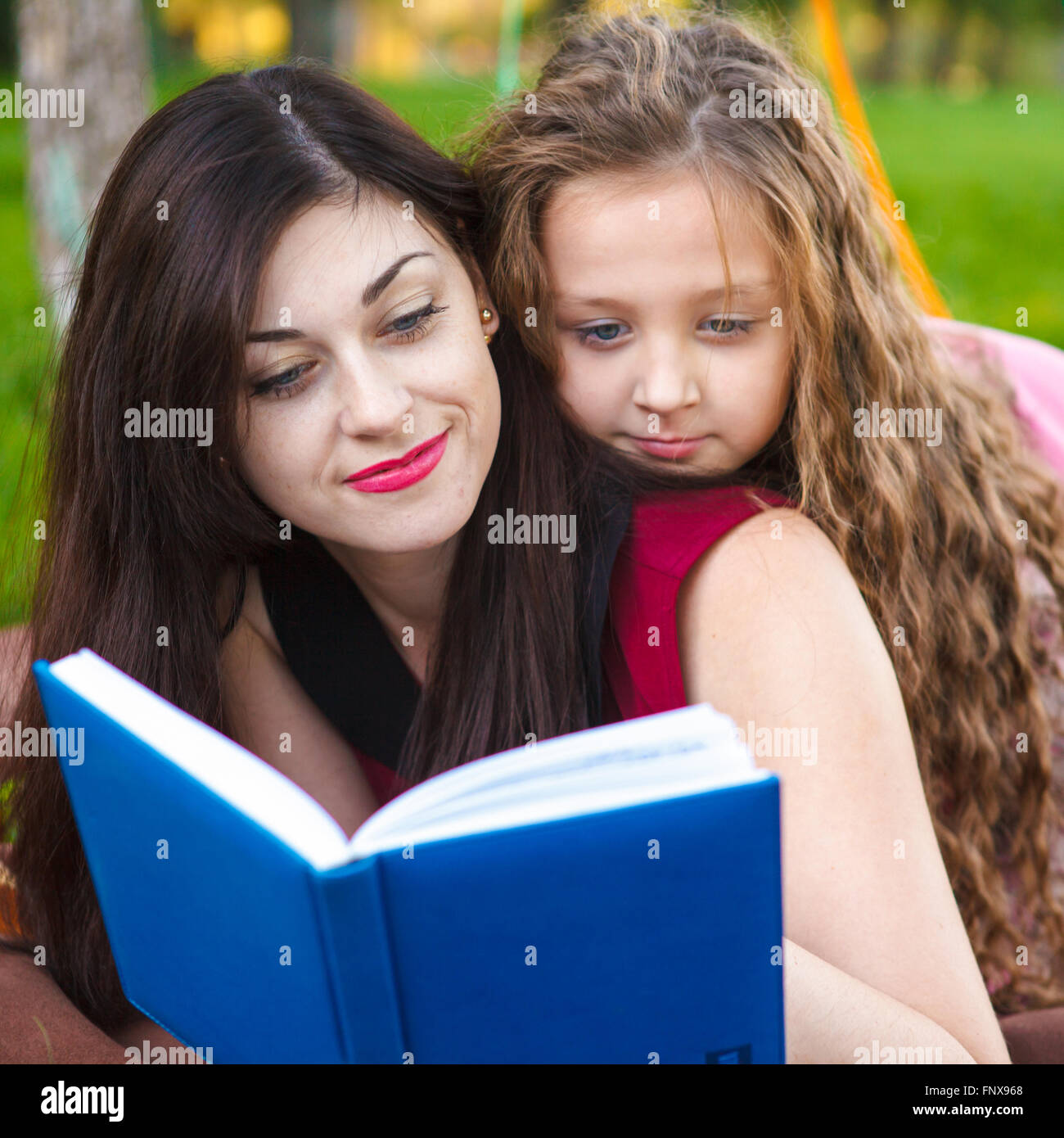 Mom And Daughter Reading A Book Lying On The Plaid In The Park Stock