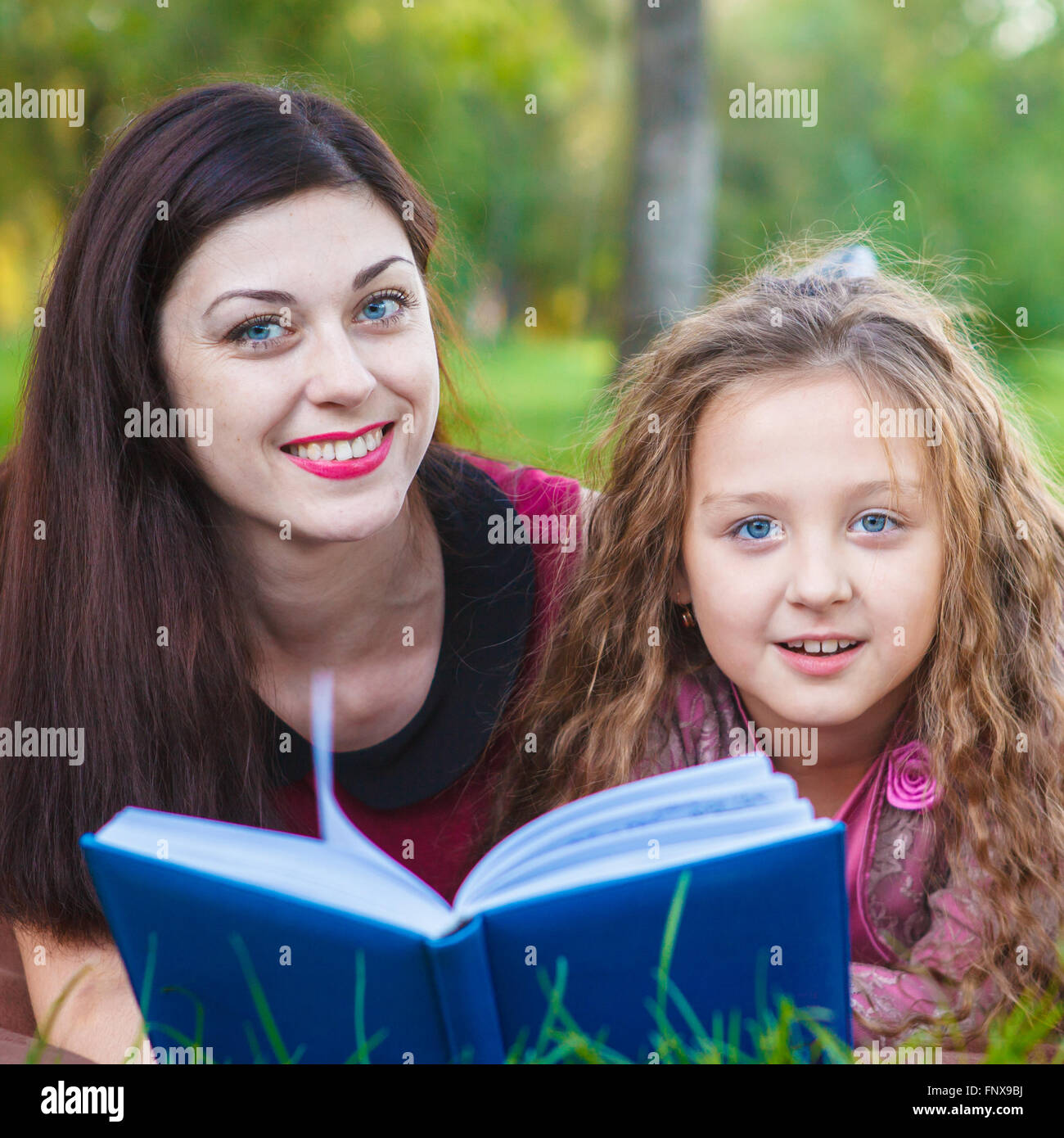 Mom And Daughter Reading A Book Lying On The Plaid In The Park Stock