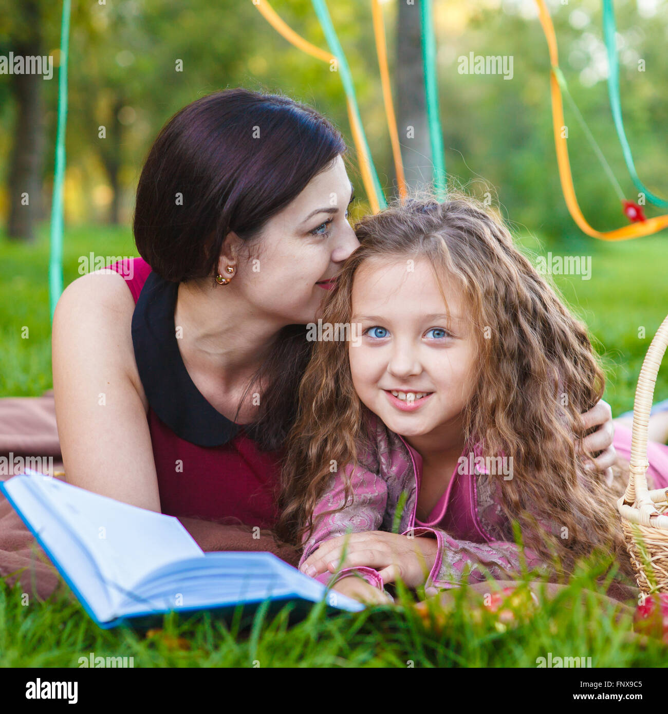 Mom And Daughter Reading A Book Lying On The Plaid In The Park Stock