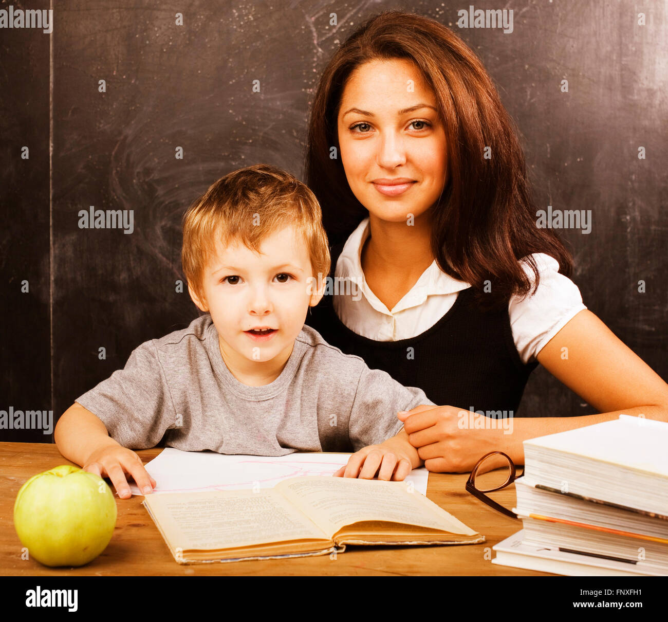 little cute boy with young teacher in classroom studying at blackboard ...