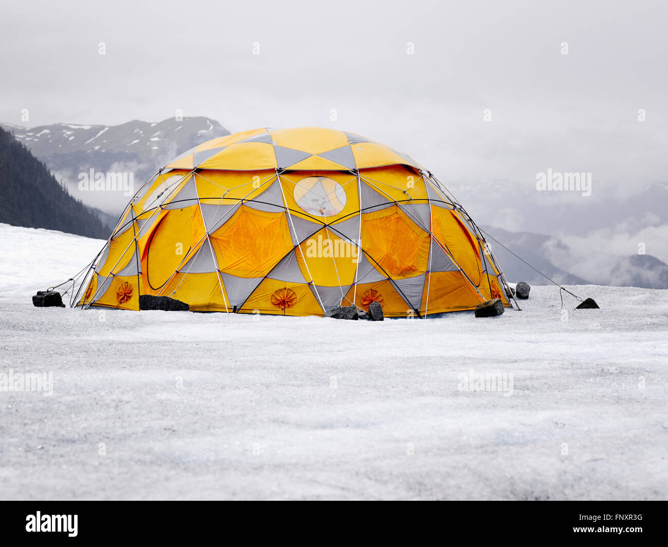 Camping in the high mountains. Orange and grey tent on the glacier ...