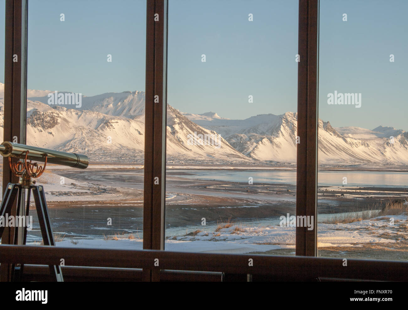 Telescope looking out through windows at lake and snowy mountain ...