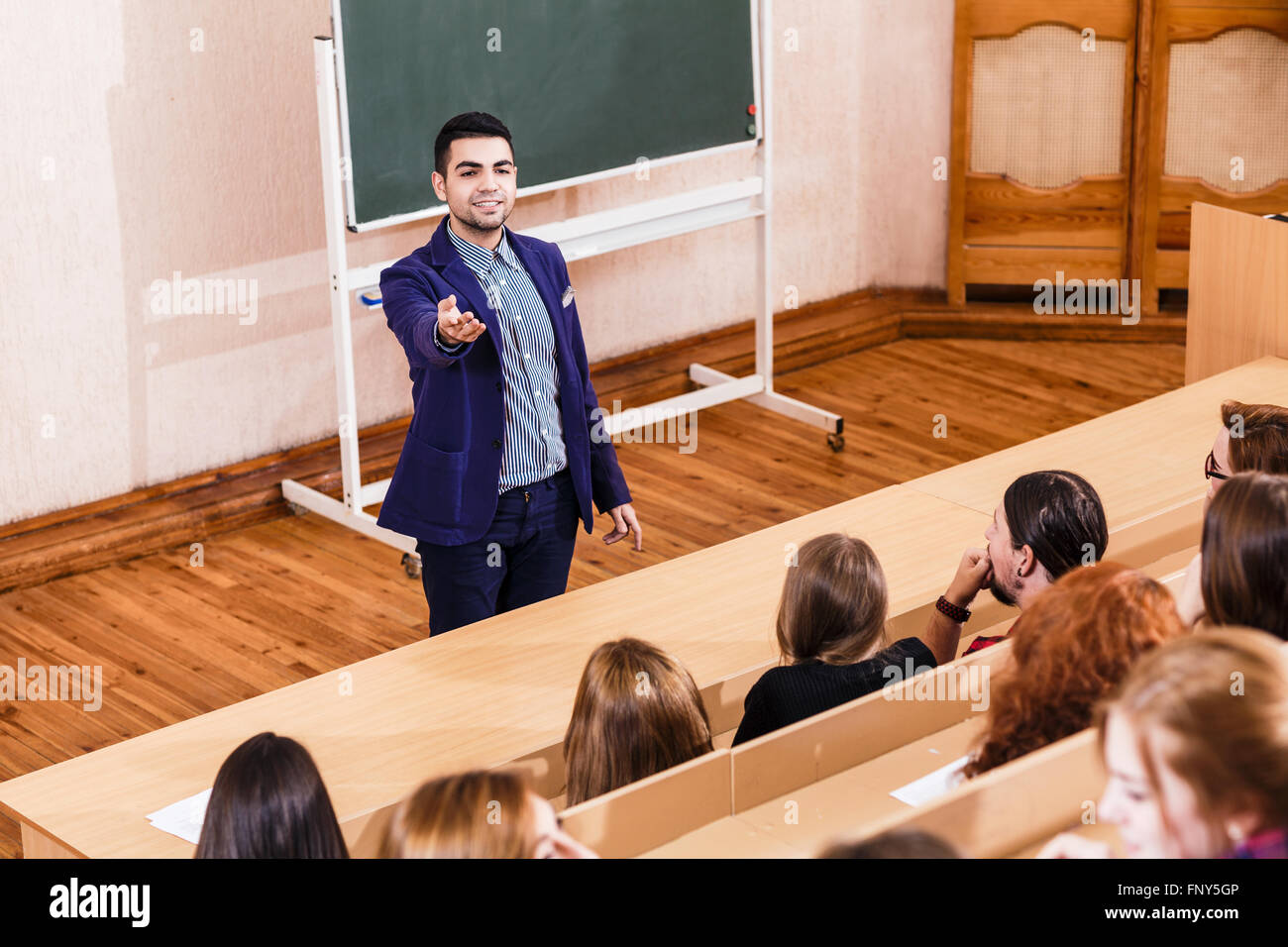 Young teacher explaining something to students in classroom Stock Photo ...