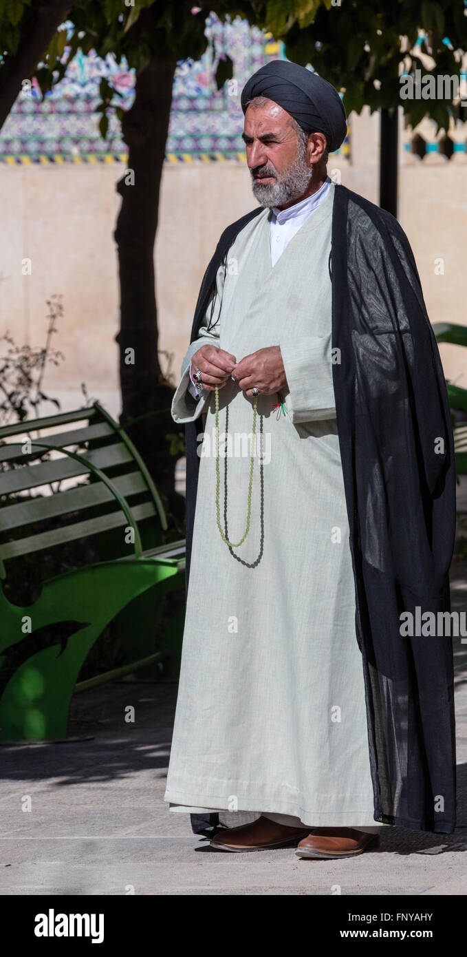 Mullah in turban and robe with worry beads stands in courtyard of Khan ...