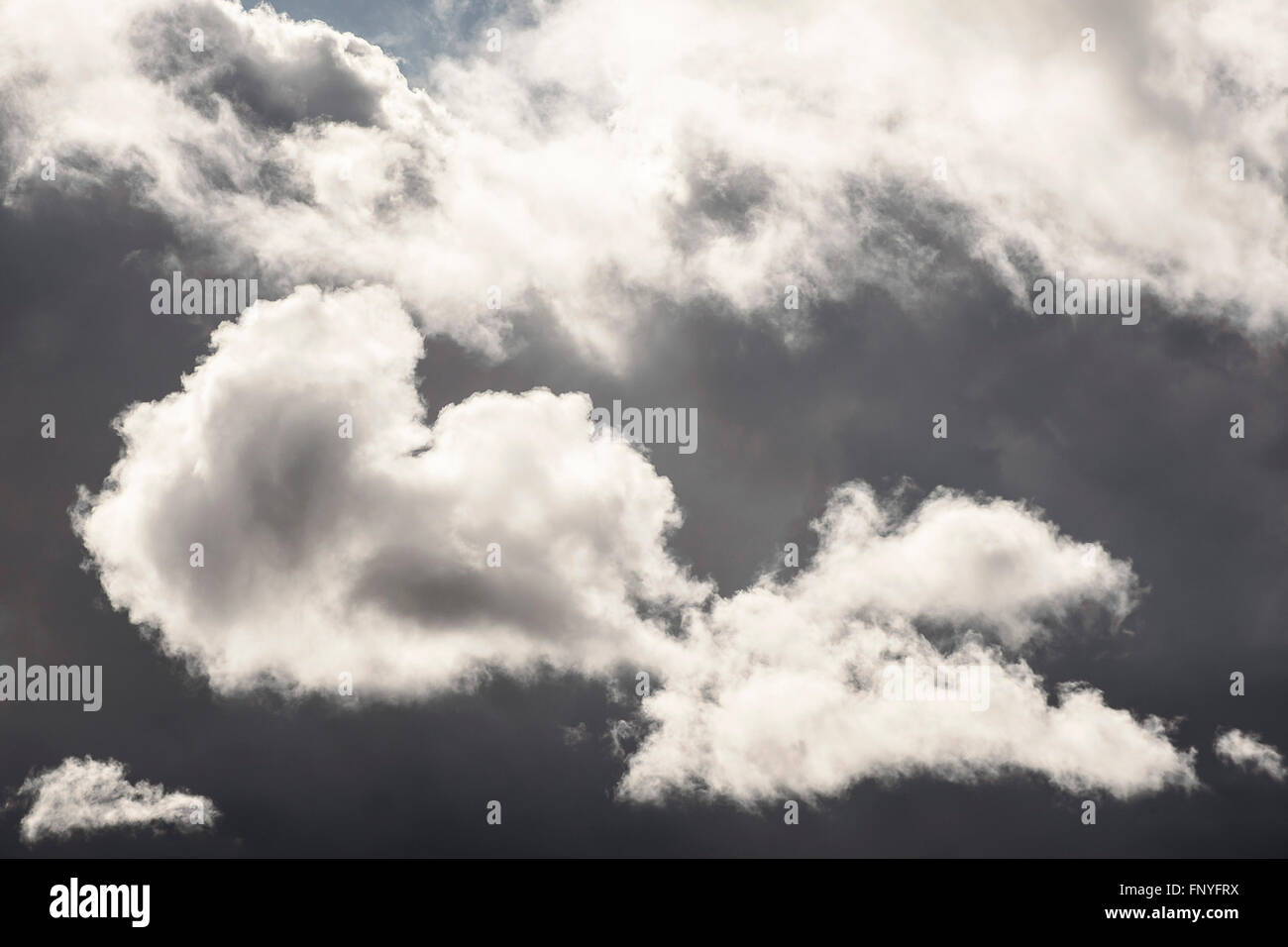 Dramatically sun lit clouds move across a bright blue sky with grey ...