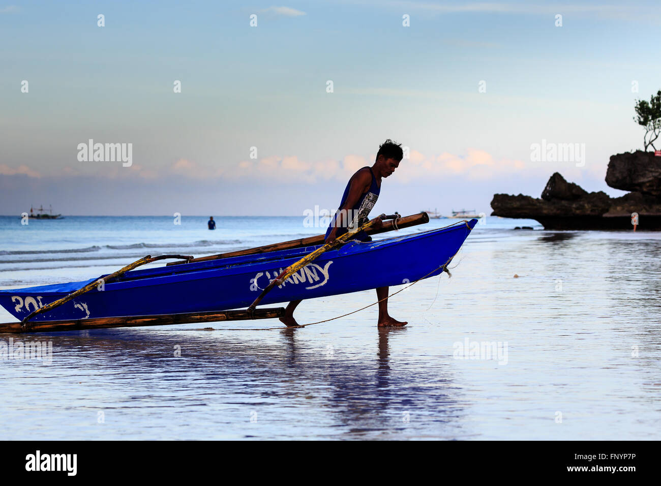 Man pulls small outrigger boat out of water onto beach Stock Photo - Alamy