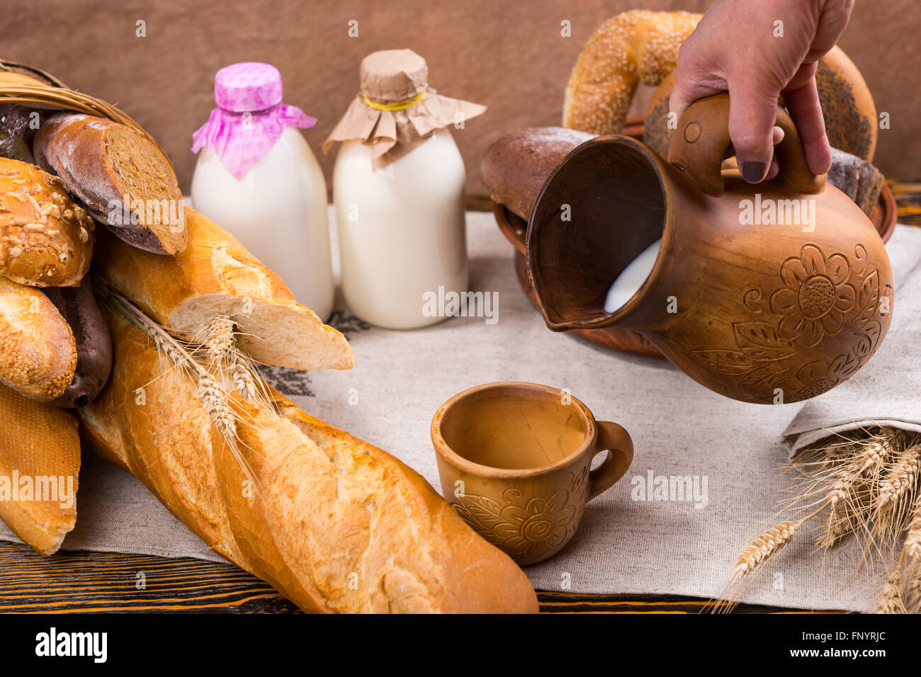 Hand pouring milk into wooden cup surrounded by bottles, loaves of ...